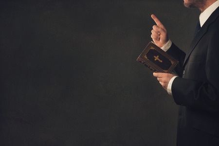 41905004 – a standing man in suit with a bible and a wagging finger ...